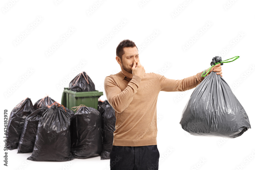 Young man holding a smelly garbage bag and covering his nose near a ...