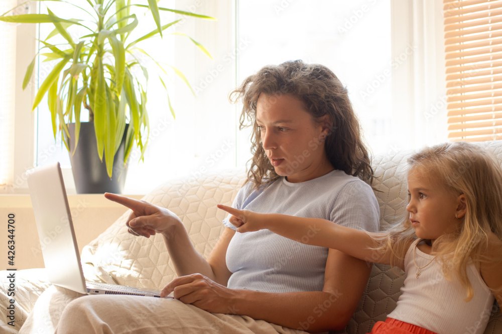 Single mother teaching little daughter using laptop computer, pointing ...