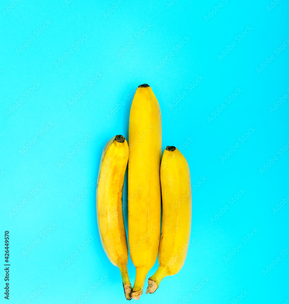 Top view. Three yellow bananas on a blue background. One of the bananas ...