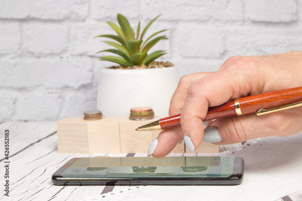 Female accountant uses mobile phone with pen to calculate profit and ...