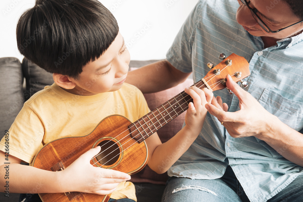 Asian father teaching his little boy to play ukulele with joy a small ...