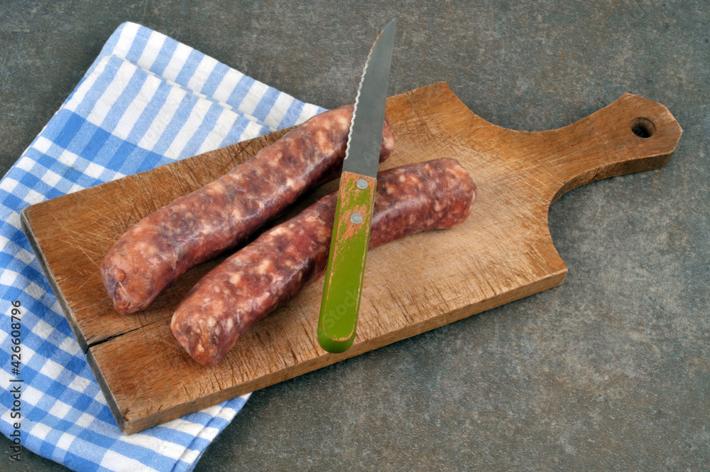 Saucisses de porc crues sur une planche à découper avec un couteau et un torchon à carreaux en ...