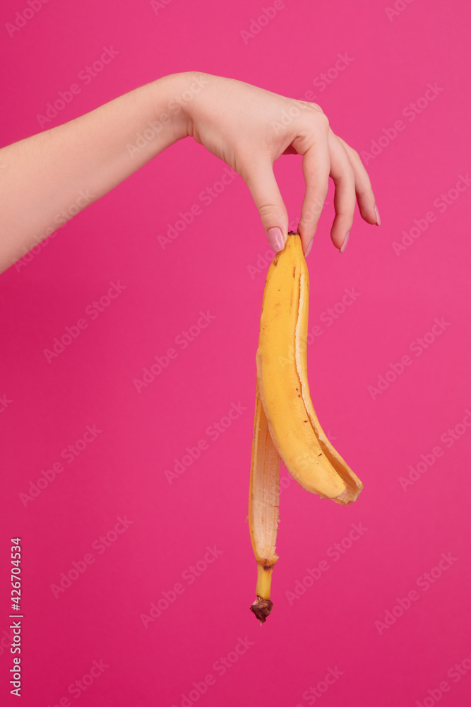 Woman's hand throwing out a banana skin on a pink background. Сoncept ...