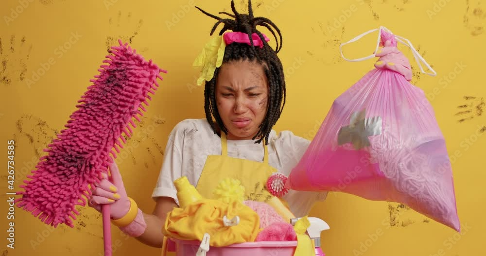Unhappy housemaid looks with aversion at garbage bag and dirty mop ...