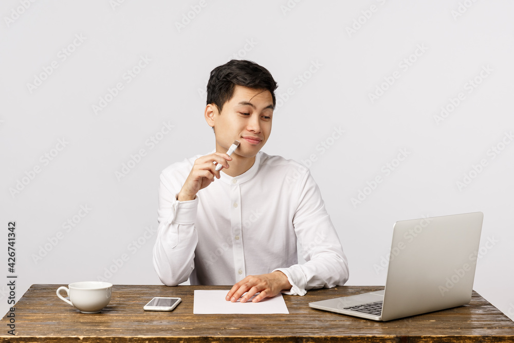 Pleased handsome young asian male entrepreneur, office worker sitting desk, smiling touched ...