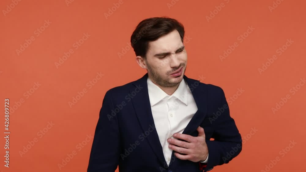 Young bearded guy in black suit grimacing from sudden pain, symptoms of ...