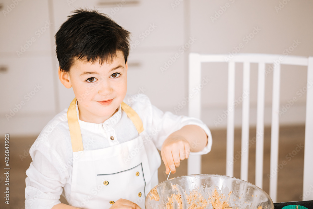 Little boy in cook chef clothes makes muffins in the kitchen. Child ...