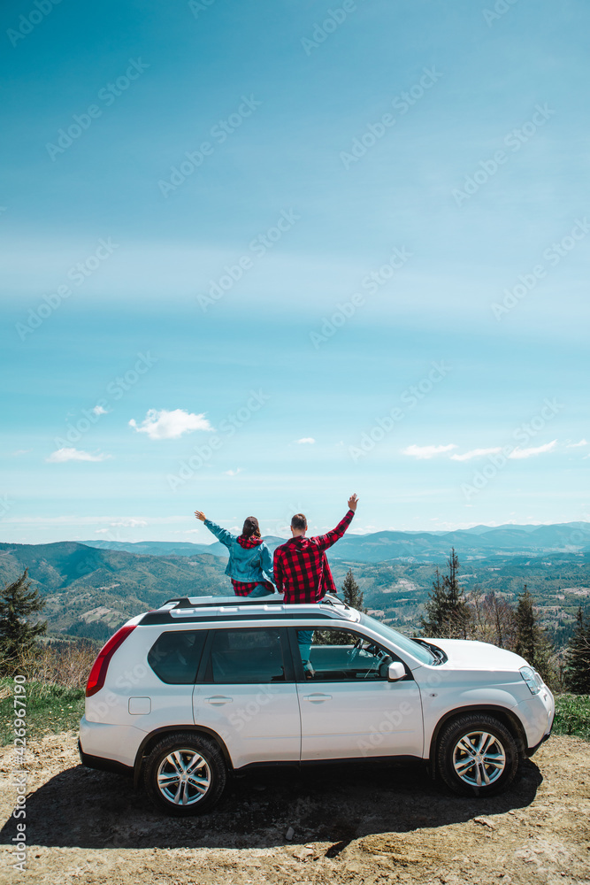 young woman sitting on the top of the suv car at mountain peak enjoying ...