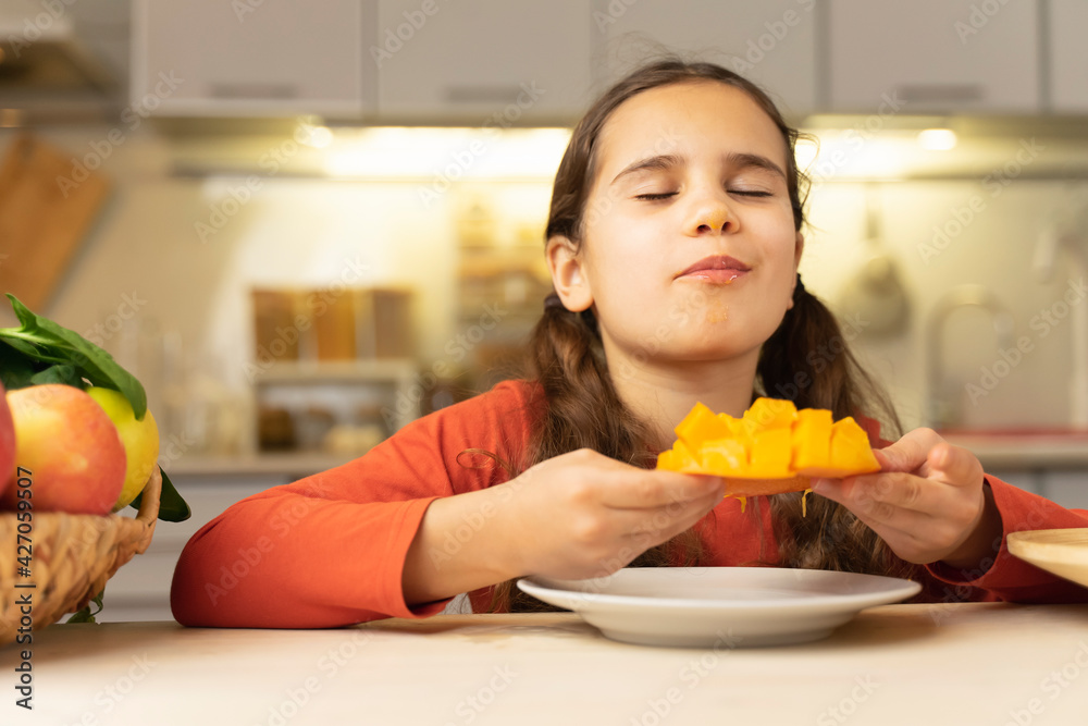 Cute child girl is happy to eat mangoes. Schoolgirl joy tasty eating ...