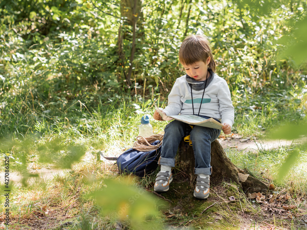 Little explorer on hike in forest. Boy with binoculars sits on stump ...