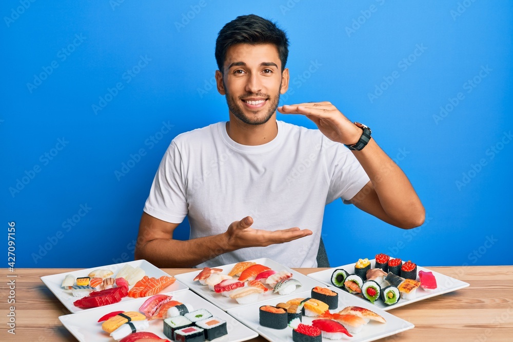 Young handsome man eating sushi sitting on the table gesturing with ...