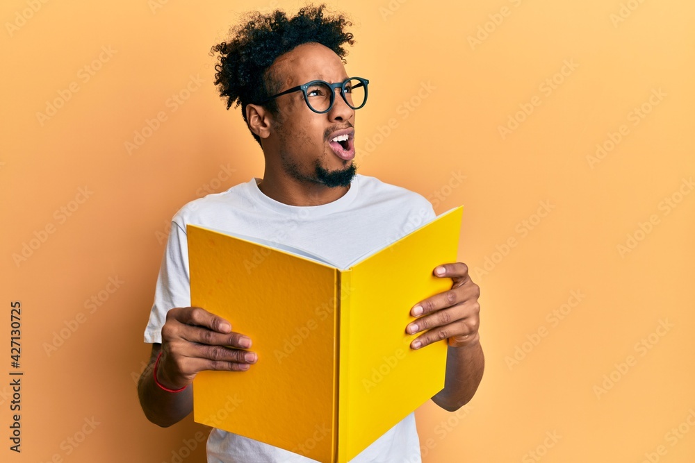 Young african american man with beard reading a book wearing glasses ...