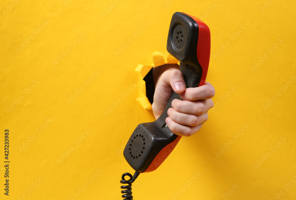 Female hand holds telephone tube through torn hole yellow paper ...