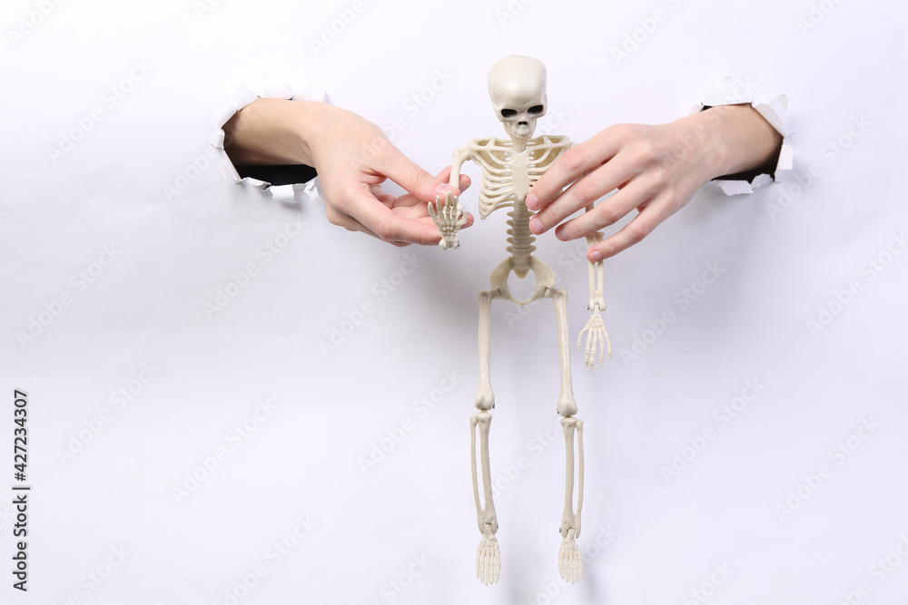 Female hands holding skeleton through torn hole white paper. Halloween ...