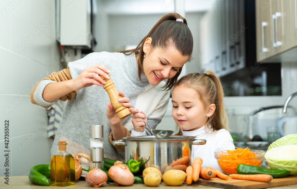 Little daughter helping cooking soup and mother add pepper to pan Stock ...
