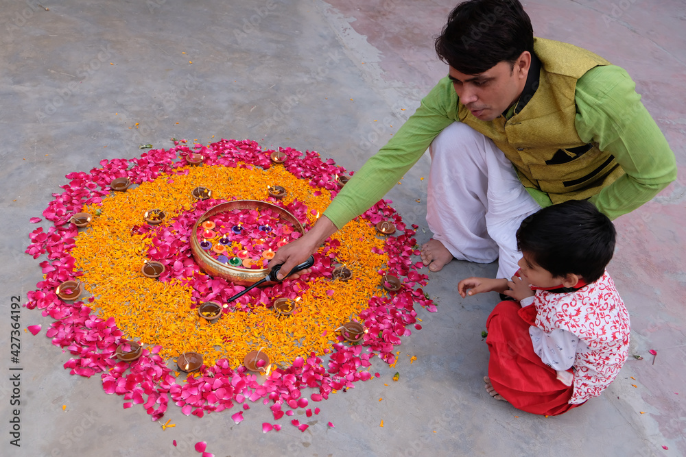Indian male with his son creating rangoli using candles, marigold and ...