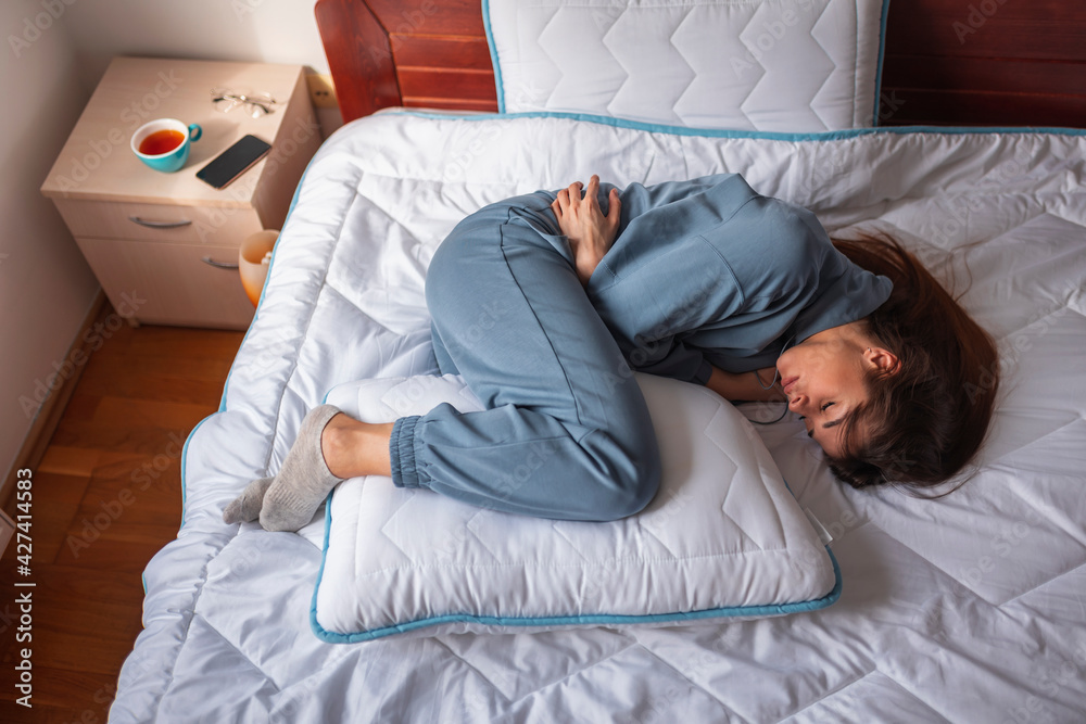 Curled up woman lying in bed with stomachache Stock Photo | Adobe Stock