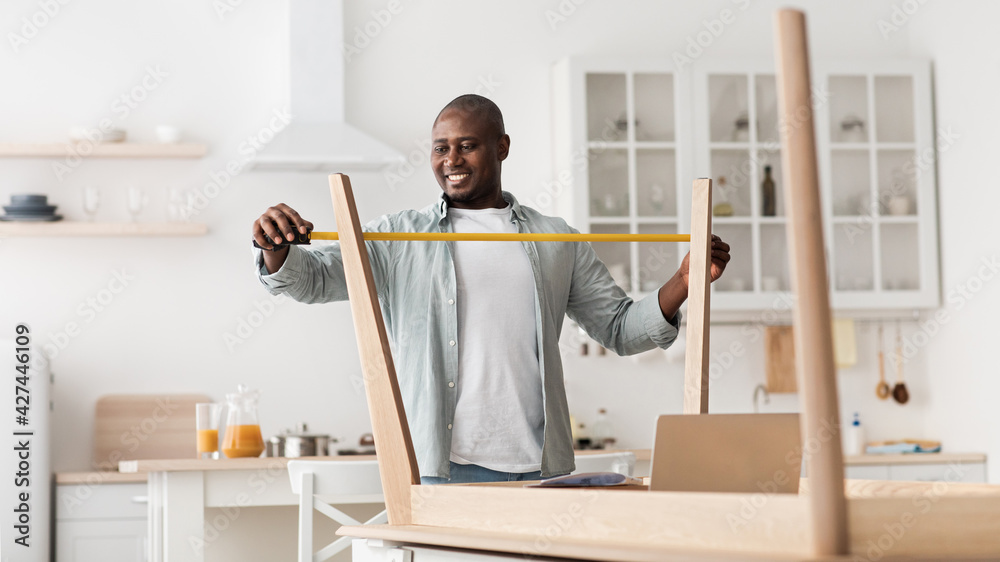Excited black man measuring furniture with roulette, assembling new ...