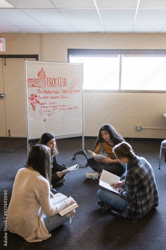 Teen girls reading on floor at book club meeting in community center ...