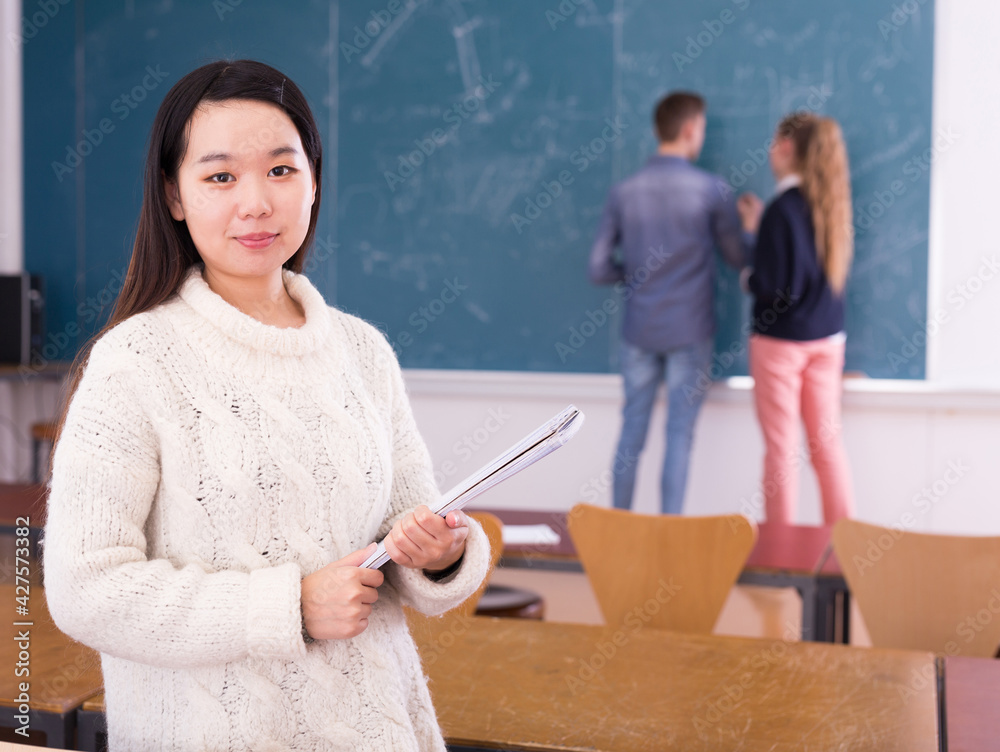 Smiling Chinese teenage girl student standing in classroom with ...