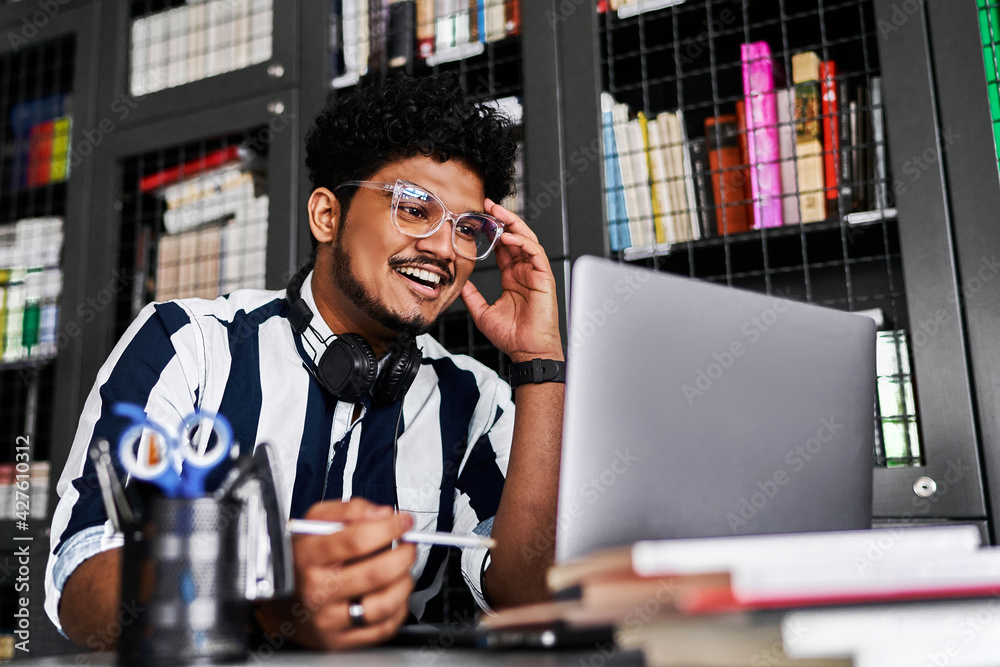 A smiling Indian teacher, a student at a computer, looks at a laptop ...