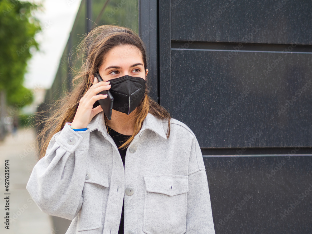 Mujer joven con mascarilla usando y hablando por su teléfono móvil ...