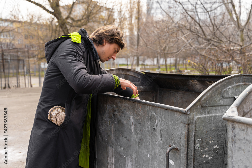 hungry young man looking for food in trash containers on the street ...