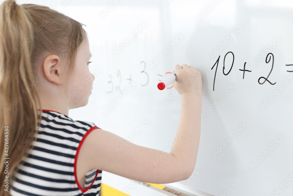 Little girl writes math examples on white board Stock Photo | Adobe Stock