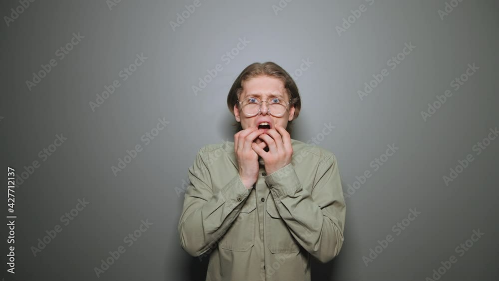 Portrait of a scared young man in shirt and glasses on gray wall ...
