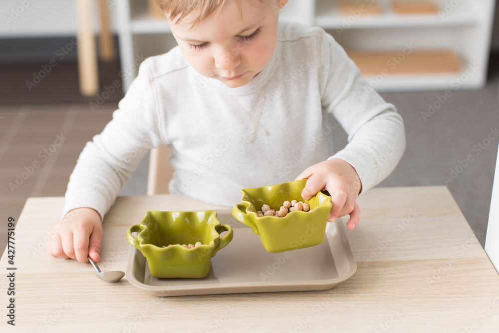Little boy pouring beans into container at Montessori preschool Stock ...