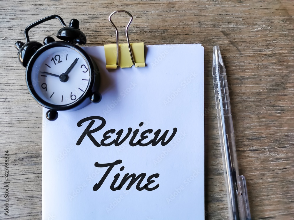 Text REVIEW TIME written on white paper with a pen and alarm clock ...