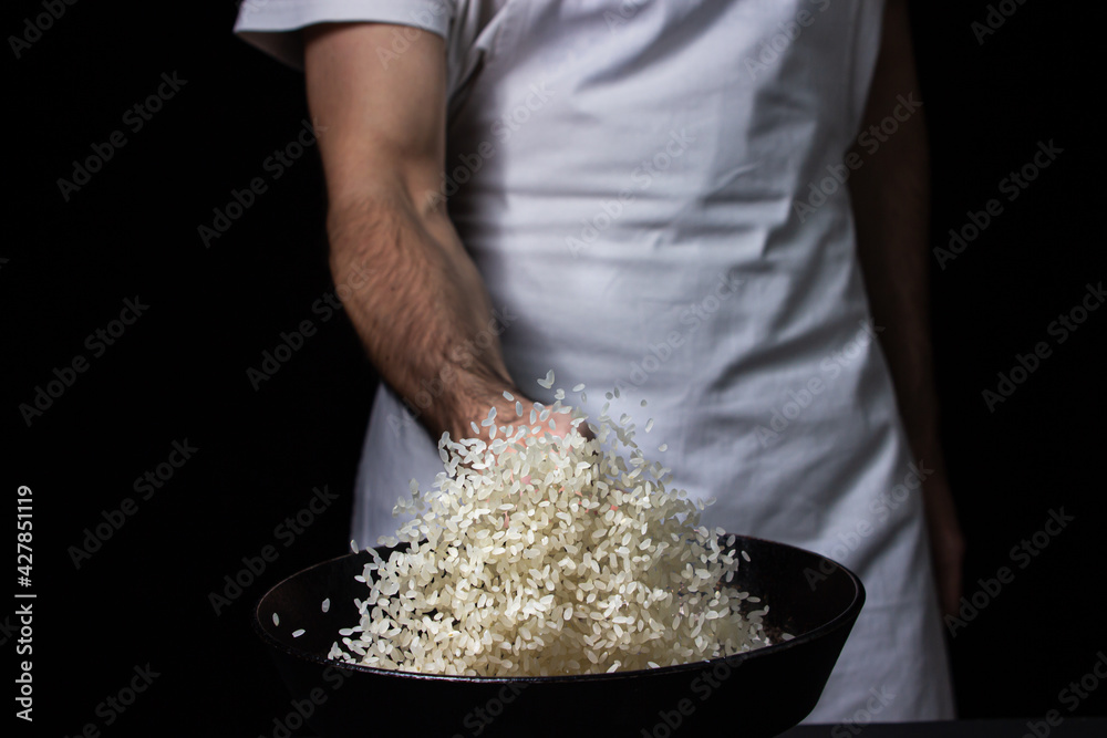Toss the rice in the skillet. The cook is throwing rice on a black ...