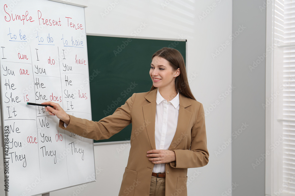 English teacher giving lesson on simple present tense near whiteboard ...