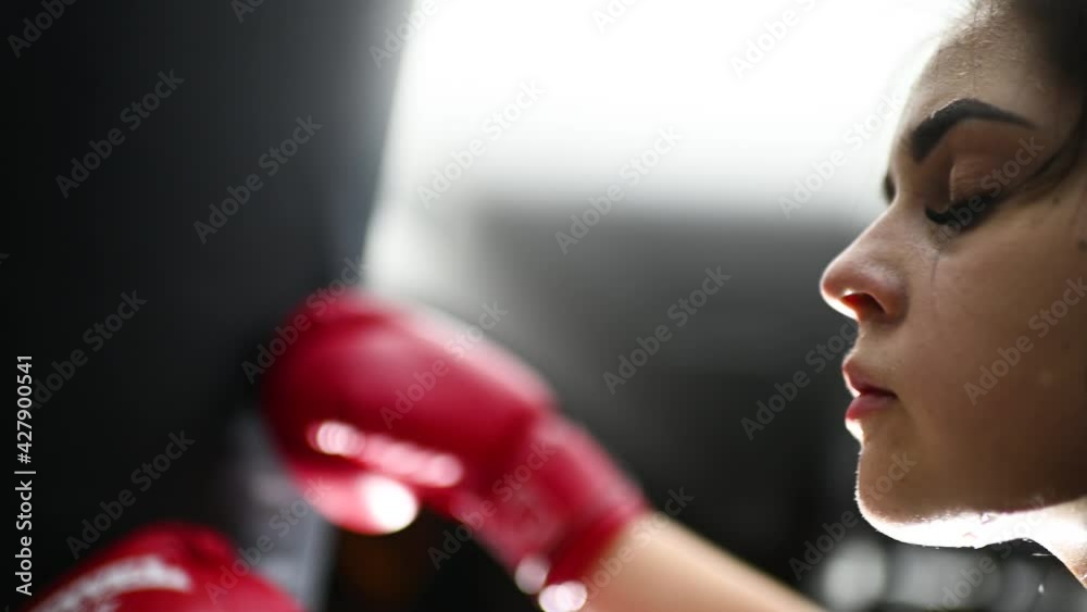 pretty young female athlete in boxing gloves hits a punching bag. Beads ...