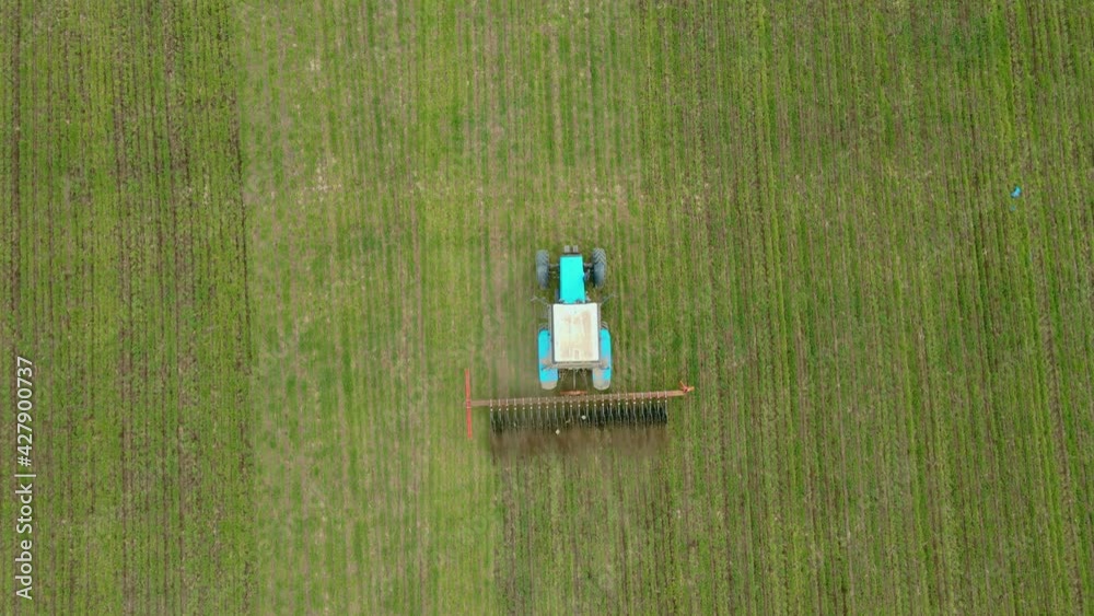 Top down view on agronomic tractor with rotary harrow plowing crops for ...