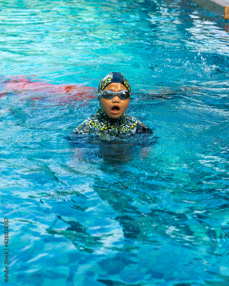 Young girl wearing hijab and Muslim swimming wear in the pool. Happy ...
