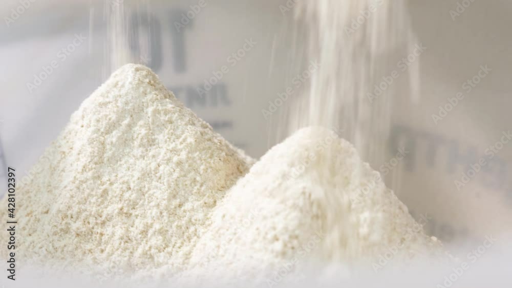 Fresh flour falls out of a trough on to a conveyor belt below inside a ...