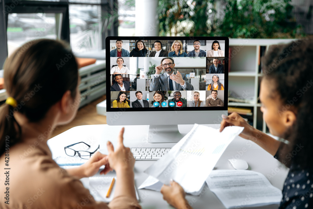 Virtual meeting online, video call. View over shoulders of two women to ...