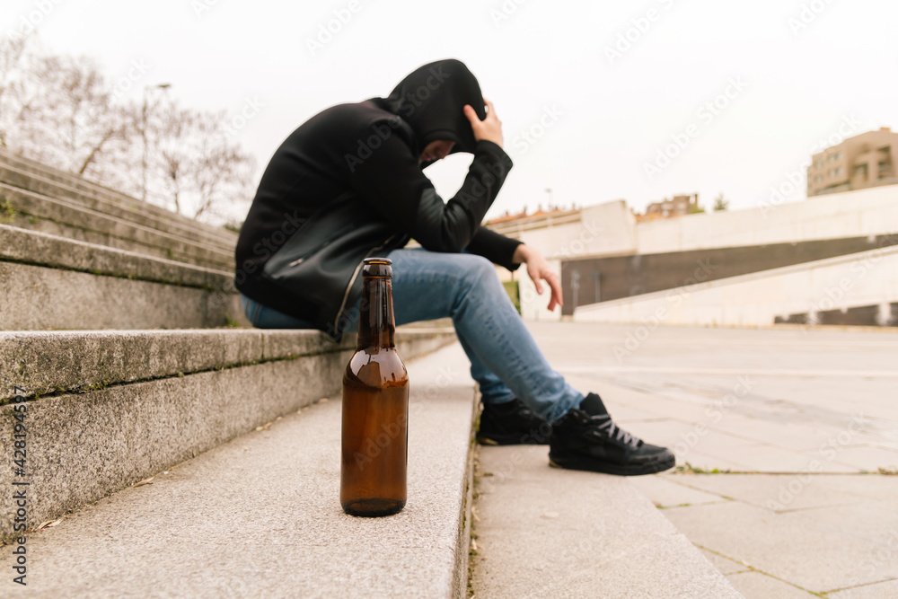 Close-up of a beer bottle on the floor with a drunk young man crying ...