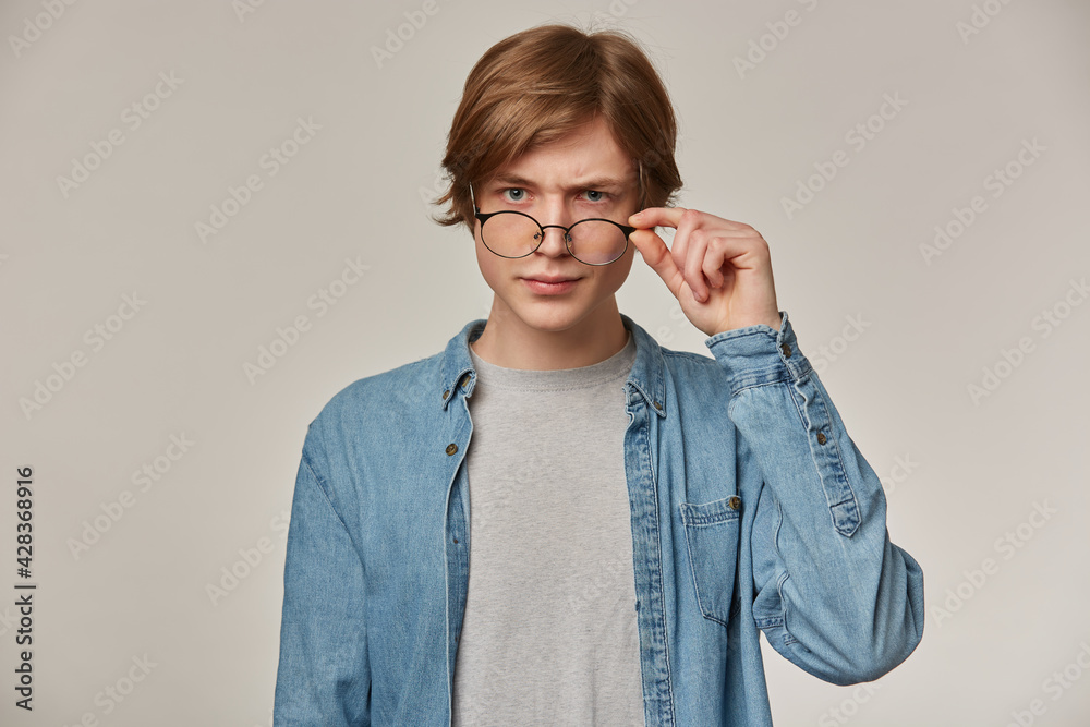 Portrait of serious, frowning male with blond hair. Wearing denim shirt ...