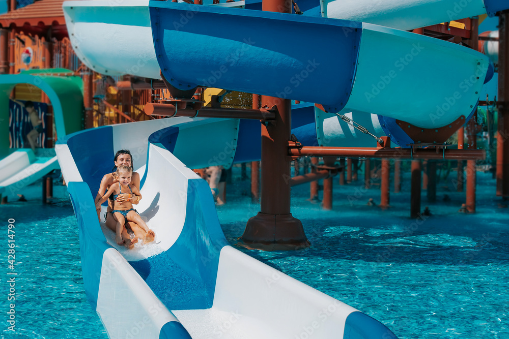 Little girl in swimsuit goes down the blue slides to the pool, Mom and ...