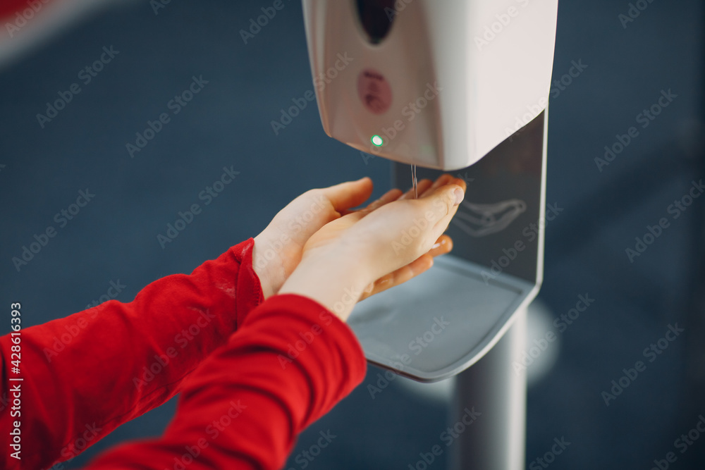 Child boy kid using automatic alcohol gel dispenser spraying on hands ...