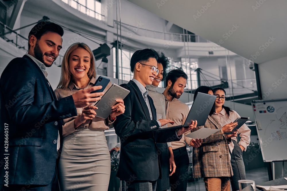 A group of business people use digital tablets, laptops, phones and ...