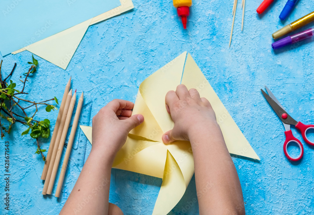 Step-by-step making of a paper weather vane by a child on a blue ...