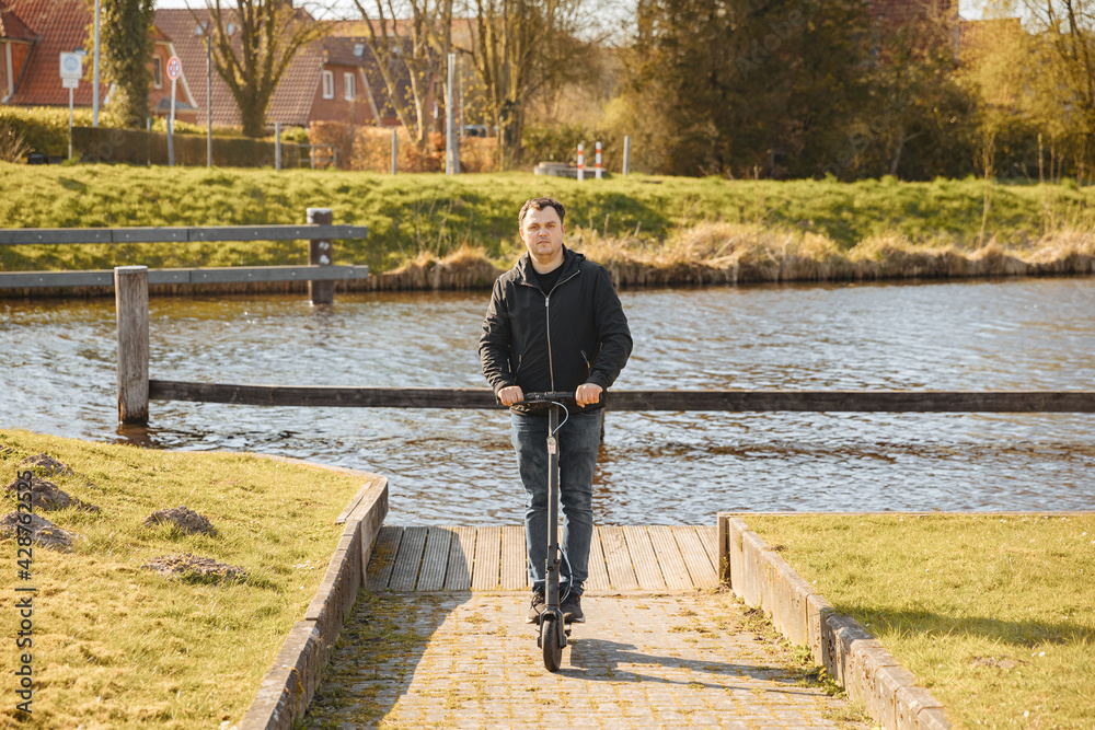 Man drives an electric scooter along a canal in the Netherlands. Person ...