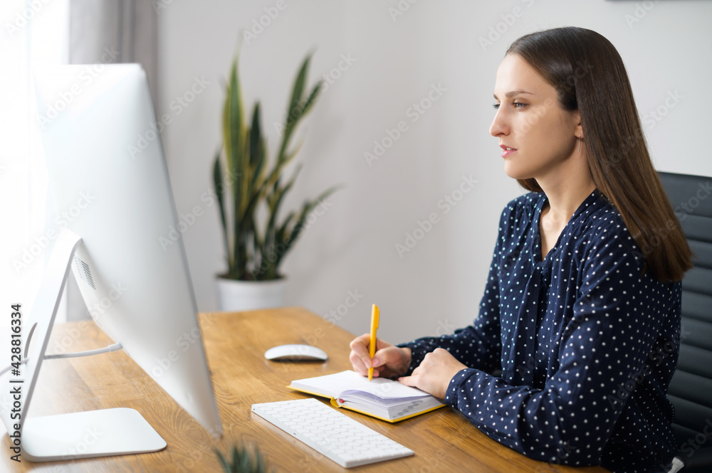 Focused female employee takes notes in notepad sitting at the desk in ...