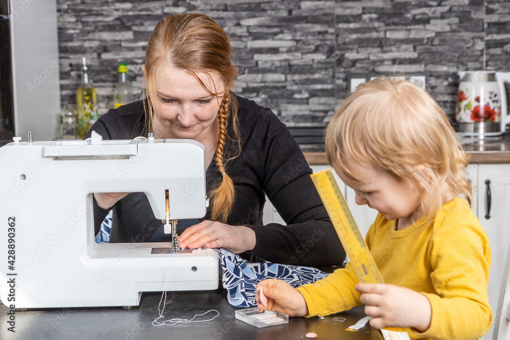 Young mother is sewing and her son is plying with tailoring supplies ...