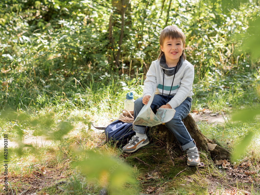 Little explorer on hike in forest. Boy with binoculars sits on stump ...
