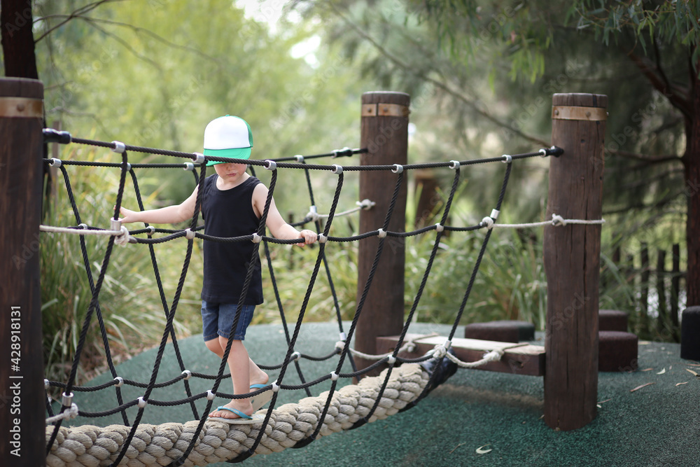 Little boy walking across rope bridge in beautiful outdoor playground ...