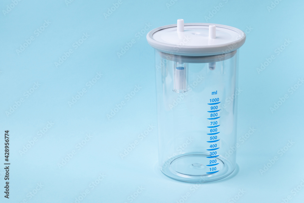 Plastic canister from medical suction machine on blue backdrop. Part of ...